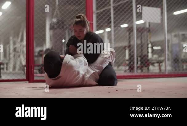 Muslim female fighter performing triangle choke while lying on floor and fighting opponent ...