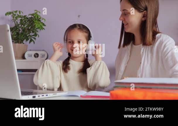 Brown haired little girl with pigtails sitting in front of laptop with her mother woman help ...