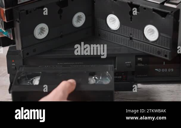 Male hand inserts VHS cassette into a VCR Video recorder. Black vintage ...