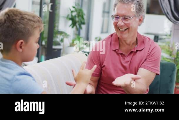 Happy caucasian grandfather and grandson sitting on sofa and using sign ...
