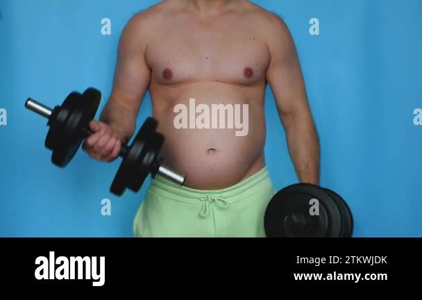 A fat man with a big fat belly with dumbbells shakes his hands, on a ...
