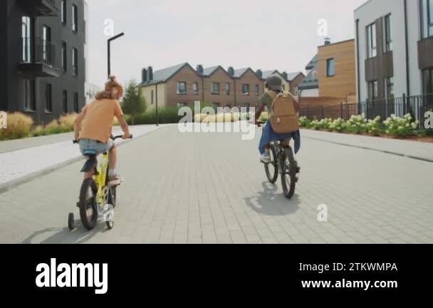 Full rear shot of two 9-year-old children in casual clothes pedaling on ...
