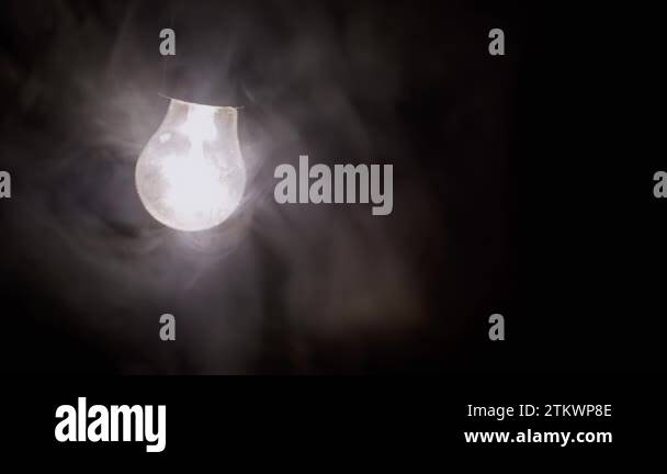 One Hanging, Glowing Light Bulb in Thick Smoke on a Black Background ...