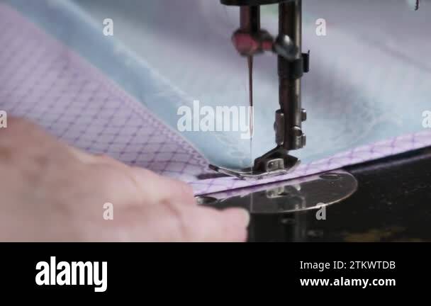 An aged seamstress sews at a traditional sewing machine at home in slow ...