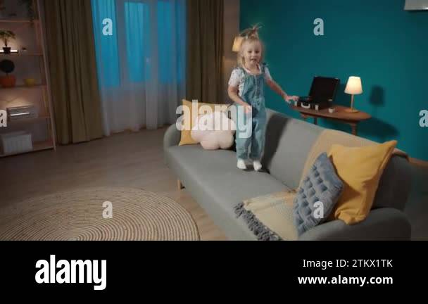 Little girl jumping on the couch in the living room, laughing and ...