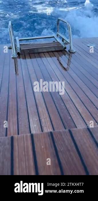 slipstream behind and splashing water on the wooden dock ladder of the ...