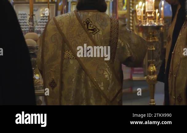 An Orthodox priest in traditional gold vestments performs a Christian ...