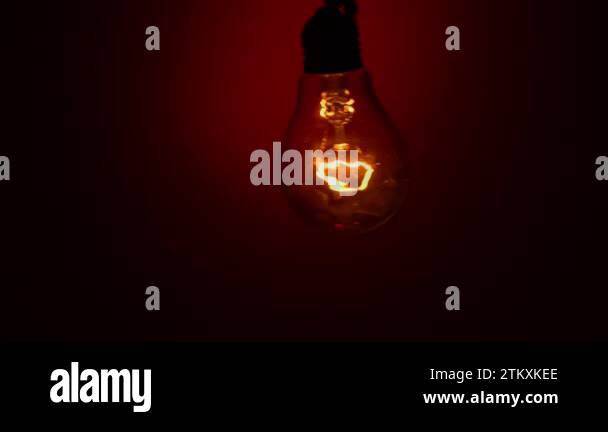 Light bulb staggers on a red background in the dark. Slow turning on ...