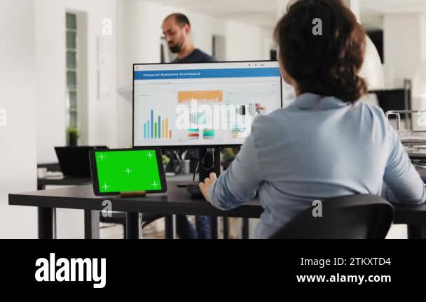 Analyst working at office desk with greenscreen shown on tablet ...
