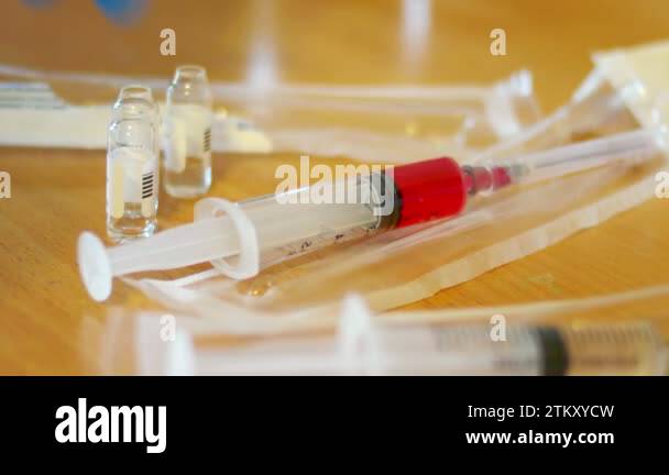 Syringe with red liquid and empty vials on table closeup. Woman in blue ...