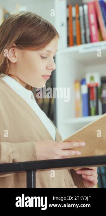 Vertical Screen: School girl in casual wear standing by bookshelves and ...