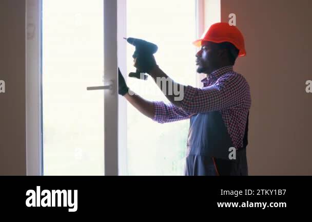 African construction worker installing window in house. Handyman fixing ...