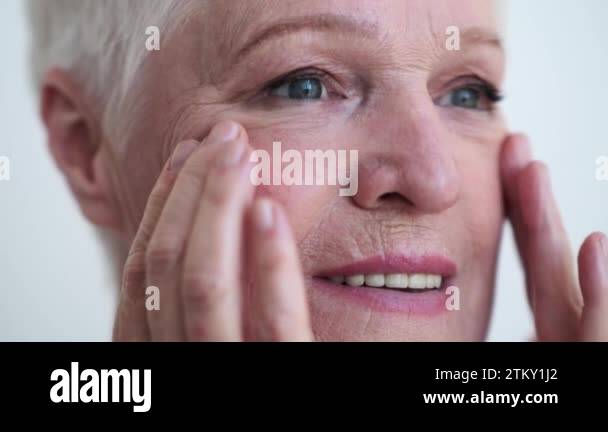 Elderly woman gently touches face with a smile of contentment. Her ...