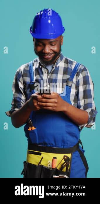 Vertical video: Construction worker texting messages on smartphone app, using social media ...