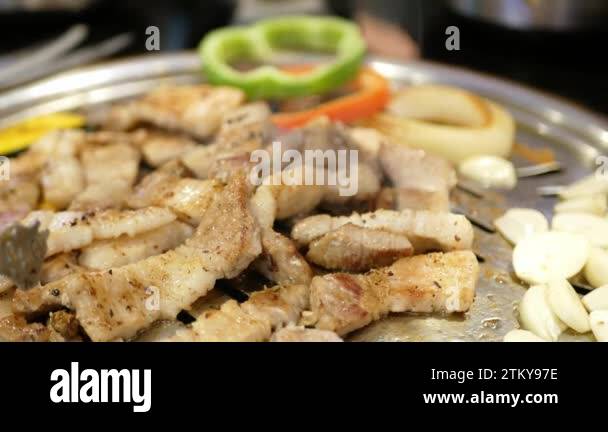 Close up shot of hand cooking Korean grilled pork belly meat on iron ...