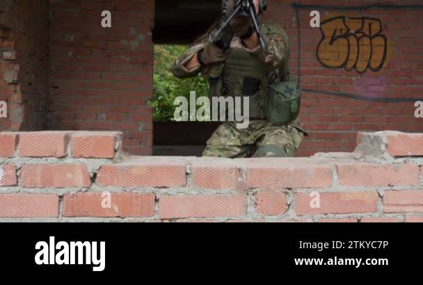 female military sniper in camouflage in a destroyed brick building, she ...