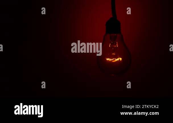 Light bulb flashes on a red background in the dark. Slow turning on and ...