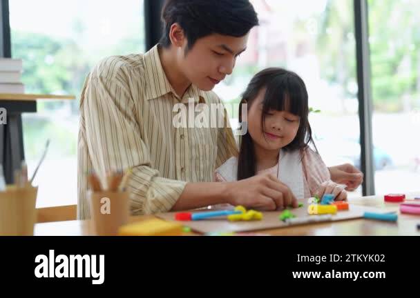 A cute looking Asian girl doing a drawing activity with a male teacher ...