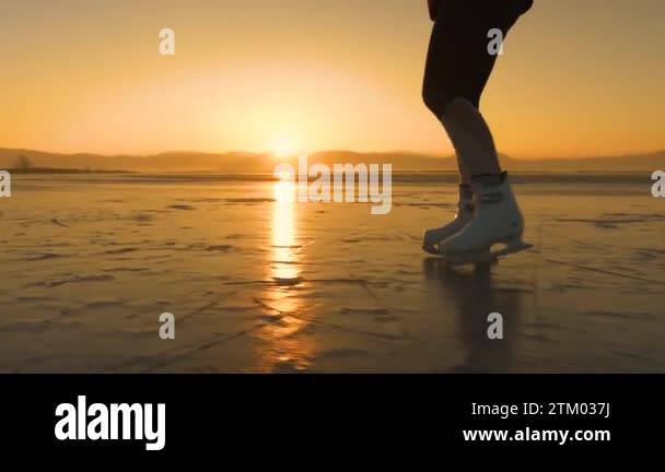 LENS FLARE, SILHOUETTE: Lady with white ice skates skating in golden ...