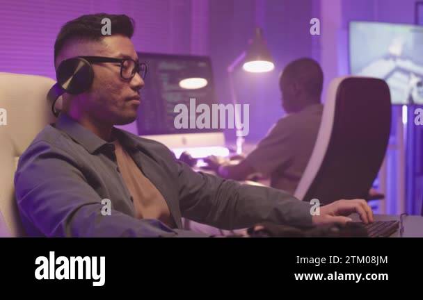 Waist up slowmo of Asian man in headphones using mouse and keyboard while playing video game on ...