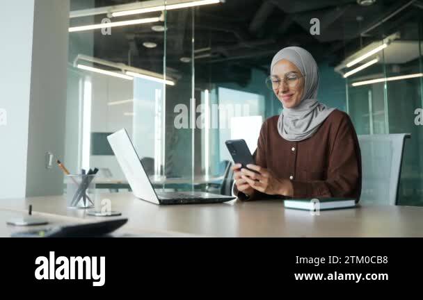 Positive young muslim businesswoman in hijab hold smartphone scrolling ...