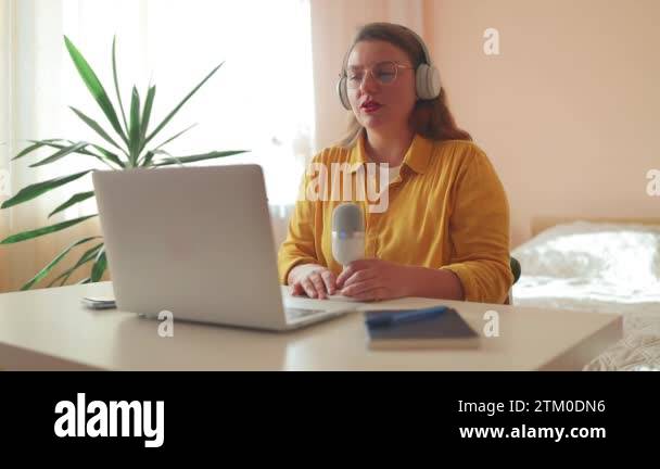 Woman recording a podcast on her laptop computer with headphones and a ...