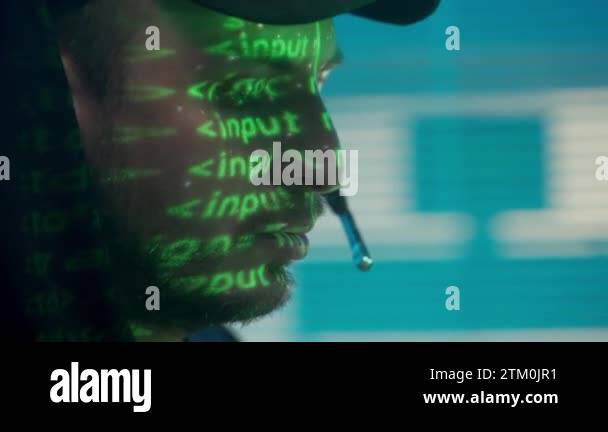 Hacker with headset working on a computer, a line of program code is reflected on his face. A ...