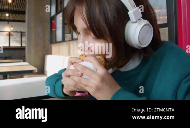 A teenage girl in headphones eats a hamburger - youth addiction to ...