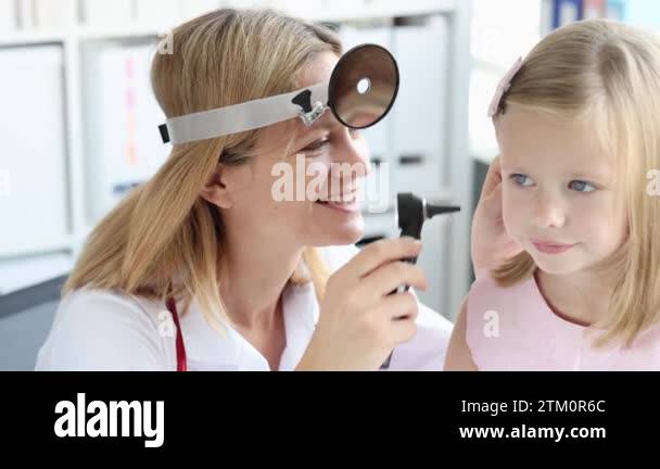ENT woman conducts physical examination of ear with otoscope of little ...