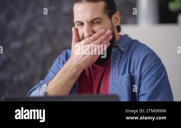 young guy worker freelancer working at laptop typing tired rubbing eyes ...