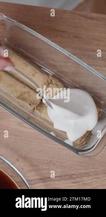 A top-down view of the preparation of tiramisu cake. The woman is ...