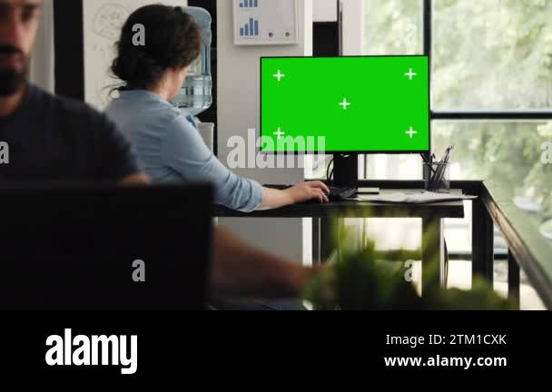 Businesswoman examining desktop with greenscreen at office desk in ...