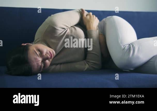 Deeply upset brunette woman lying down on sofa and touching her belly ...