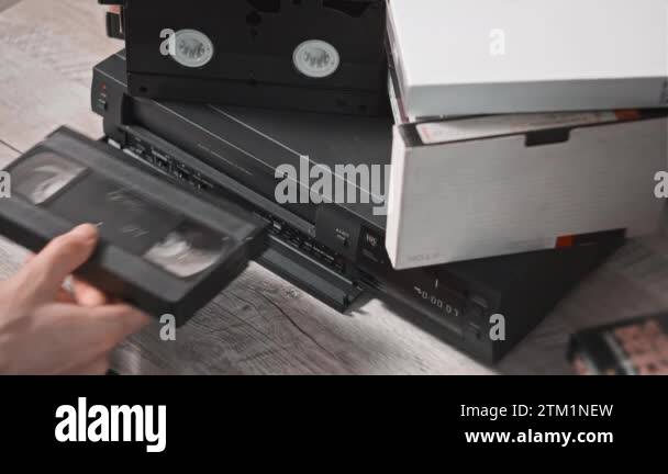 Male hand inserts VHS cassette into a VCR Video recorder. Black vintage ...