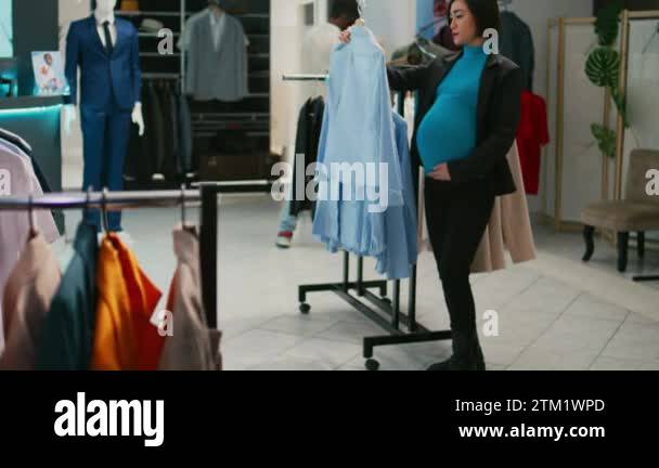 Asian woman with baby bump shopping for clothes in department store at ...