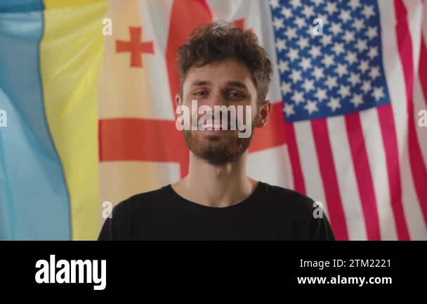 A smiling curly-haired man stands against the background of the flags ...