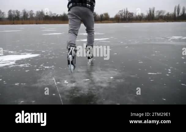Young man shod in figure skates sliding on ice surface outdoor. Guy ...