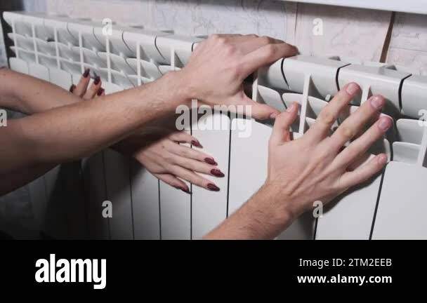 Couple warms hands on the heating radiator by the wall. Frozen male and ...