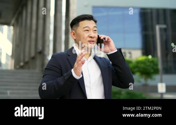 Friendly Smiling Asian Businessman In Formal Suit Talking On Smartphone
