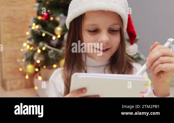 Smiling girl in red hat writing letter to Santa Claus asking for ...