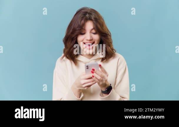 A teenage girl sits on a blue background, smiling and excited as she ...