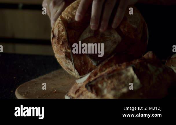 Cropped view of man baker cutting fresh loaf bread with crispy crust ...