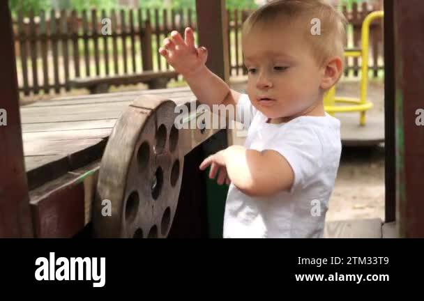 Happy smiling baby boy rotating wooden steering wheel at toy car on the ...