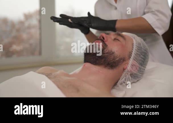 Woman's hands in black gloves applying cream on man's neck, forehead ...