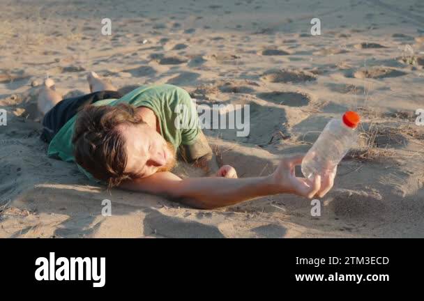 A man lies on the sand under the scorching sun in the desert. He's ...