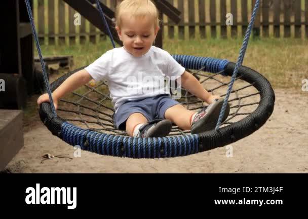 Cute smiling baby boy swinging in rope swing. Kids playing outdoors ...