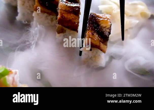 closeup of black chinese chopsticks take eel sushi from plate with cold ...