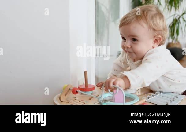 little caucasian baby girl learning to walk, pushing a wood game table ...