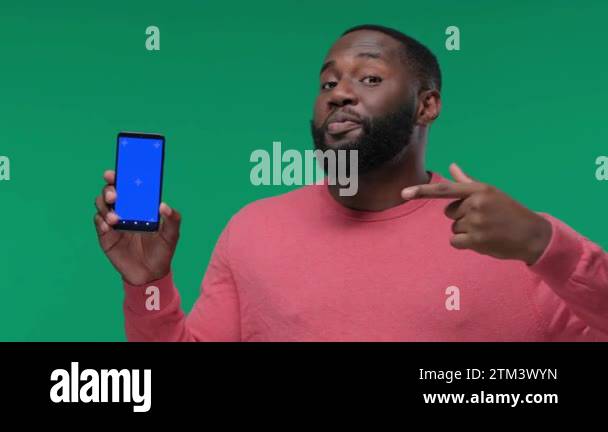 Happy young black MAN showing his phone screen with chroma key and pointing to it on Green ...