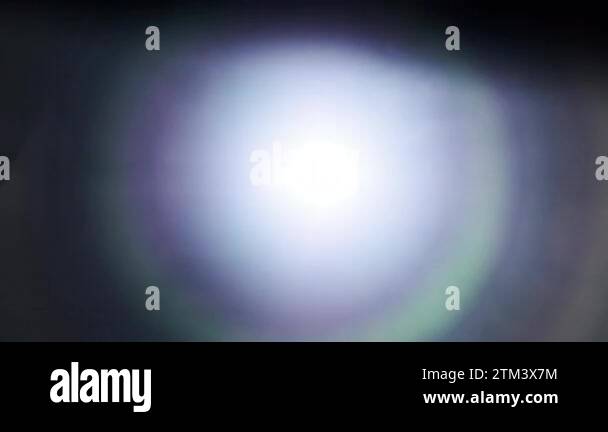 The light of a bright flashlight directed at the camera moves from side ...